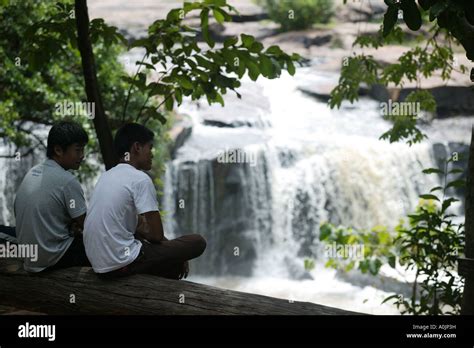 Two Men Sat On A Fallen Tree Trunk Looking Over The Waterfall In Tadtone National Park Stock