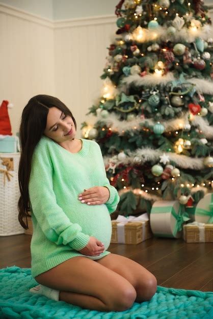 Hermosa joven embarazada decora un árbol de navidad Foto Premium