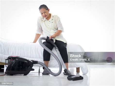 아시아 의 노인 여성 주부는 진공 청소기로 침실에서 바닥을 진공 청소기로 청소하고 피곤하고 지친 느낌 침대에 앉아서 휴식을 취하며 집에서 집안일을하는 할머니 60 64세에