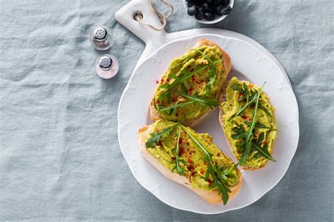 아보카도와 Arugula 샌드위치와 파프리카가 식탁에 있습니다 파란 리넨 식탁보에 있는 접시에 건강 한 아침 식사 또는 간식 0