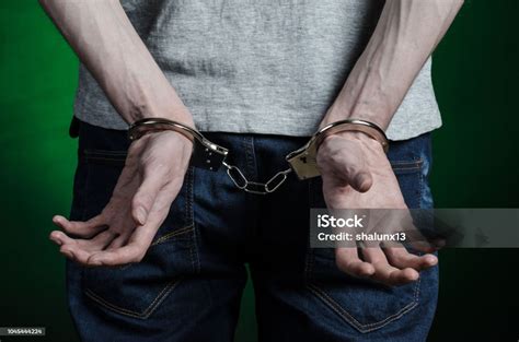 감옥과 유죄 판결된 주제 회색 티셔츠에 그의 손에 수 갑 및 스튜디오 마약 딜러 뒤에서 보기에 수 갑을 넣어 진한 녹색 배경에
