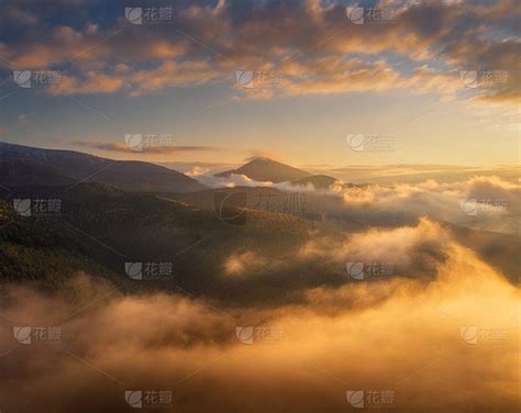 在夏天日出时，群山在云中。雾中山峰的鸟瞰图。美丽的风景有高高的岩石，森林，天空。从低云层中的山谷无人