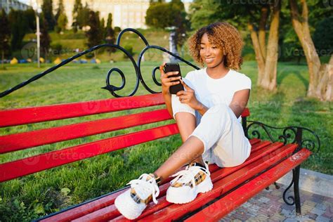 Portrait Of Young African American Woman Sitting On Park Bench With