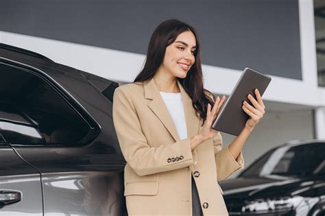 미소 짓는 자동차 판매자 베이지 색 양복을 입은 사업가가 자동차 살롱에 서서 올바른 자동차를 선택하기 위해 태블릿을 사용합니다 25 29세에 대한 스톡 사진 및 기타 이미지