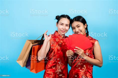 중국 드레스 데이에 치파오를 입은 두 명의 여성 빨간 봉투를 들고 종이 봉지를 들고 각각 서서 자랑하고 행복하게 웃고 파란색