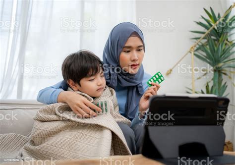 아시아 무슬림 어머니와 아픈 아들이 태블릿을 사용하면서 가정의와 화상 통화를 하며 약을 조언하고 있다 25 29세에 대한 스톡