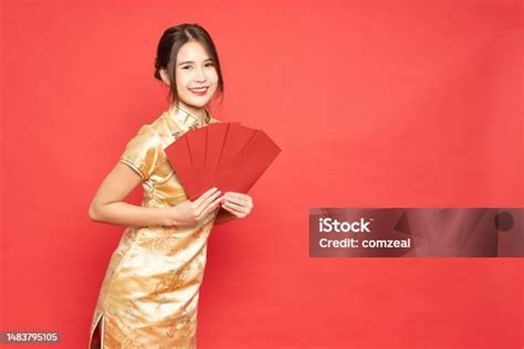 빨간 앙파오를 들고 황금빛 전통 치파오 드레스를 입은 젊은 아시아 여성이나 빨간 배경에 고립된 패킷 머니 선물 중국 설날 개념