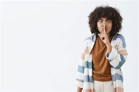 수업 중 침묵을 요구하는 입 위에 검지 손가락으로 쉬쉬 제스처를 보여주는 최신 유행의 옷에 아프로 헤어 스타일을 가진 심각한 불쾌한 아프리카 계 미국인 여성 교사 무료 사진