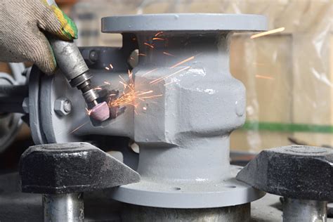 밸브의 베이스는 공장에서 조립 하기 위해 철 테이블에 장착 되 고 작업자는 연 삭 공구를 사용 하 여 회색 몸체를 연마 하 고 스파크 비행 강철에 대한 스톡 사진 및 기타