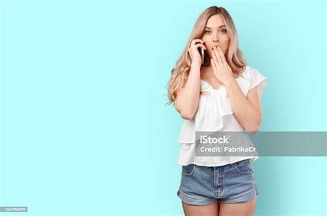 고립 된 색상 배경을 통해 전화로 말하는 충격을 받은 젊은 여성 Brand Name Smart Phone에 대한 스톡 사진 및