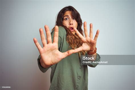 회색 고립 된 배경 위에 서있는 녹색 셔츠를 입은 젊은 아름다운 여성은 두려움 표정으로 두려워하고 손으로 제스처를 멈추고 충격에