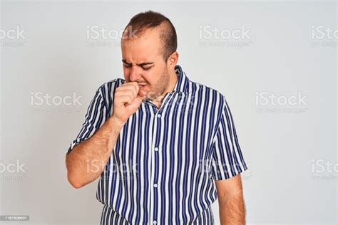 고립 된 흰색 배경 위에 서있는 파란색 줄무늬 셔츠를 입은 젊은 남자는 감기 또는 기관지염의 증상으로 기분이 좋지 않고 기침합니다 헬스케어 개념 감기와 독감에 대한 스톡