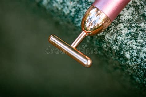 Golden T Shape Face Massager With Vibration On A Grey Granite Podium
