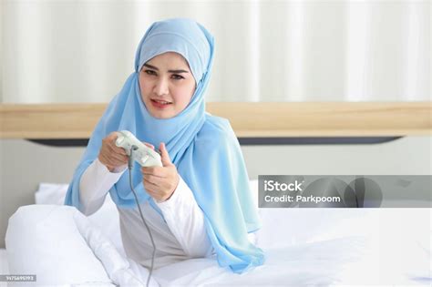 Vdo 게임 콘솔 스테이션 개념입니다 하얀 무슬림 잠옷을 입고 침대에 앉아 조이스틱을 들고 흥미진진한 게임을 하는 활동적인