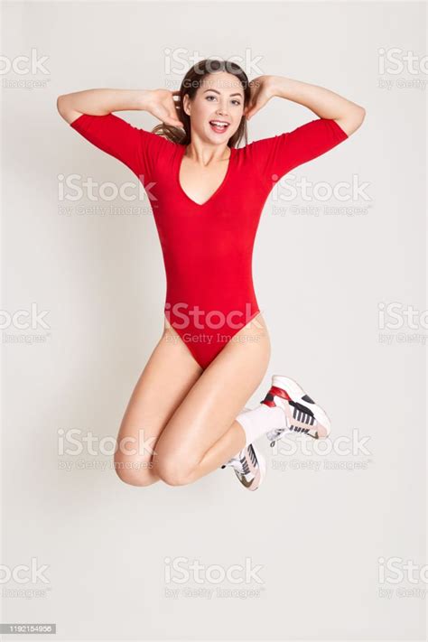 매력적인 여성이 머리에 팔을 대고 공중에 뛰어 들고 흰색 배경 위에 고립 된 포즈를 취하고 입을 벌리고 흥분한 표정을 하는
