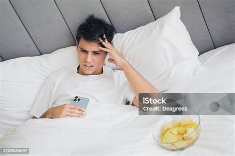 스마트폰과 간식을 들고 침대에 누워 낮에는 집에서 조용한 여가를 즐기는 젊은이 20 24세에 대한 스톡 사진 및 기타 이미지 20 24세 Brand Name Smart