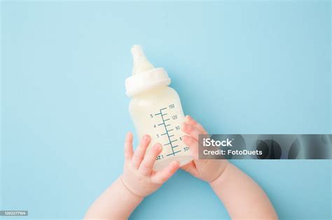 밝은 파란색 바닥 배경에 우유 병을 들고 유아 손 먹이 주기 파스텔 색상입니다 근접 촬영 시점 샷 하향하 보기 아기에 대한 스톡