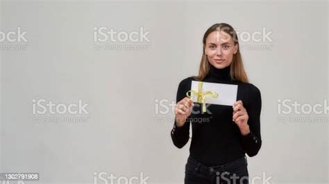 회색 배경에 고립 된 포즈를 취하면서 쇼핑을위한 상품권을 들고 검은 색 의상을 입고 있는 예쁜 젊은 백인 여성 여자에 대한 스톡 사진 및 기타 이미지 Istock