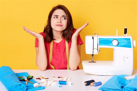 재봉틀 스티치 바늘과 흰색 책상에 앉아 Tsylist 소녀 장인 재 봉사의 스튜디오 샷 매력적인 갈색 머리 하 수도 옆으로 보이고 그녀의 장비에 문제가 있다 드레스에 대한