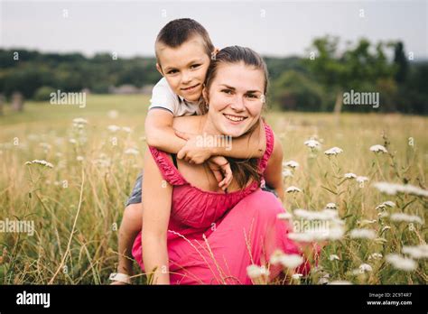 Woman Playing With Little Son In Field With Weeds And Meadow Flowers On
