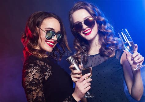 Two Young Pretty Women Wearing Black Dress Holding A Glass Of Wine And