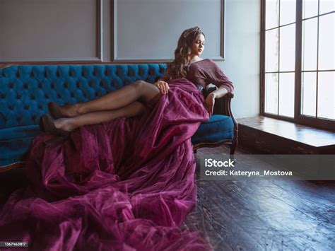 긴 보라색 여왕의 드레스와 크라운에 아름다운 젊은 예쁜 귀여운 여자 공주 의 초상화 긴 머리와 파란색 벨벳 소파에 앉아 메이크업