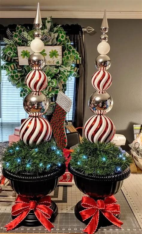 Two Christmas Decorations On Top Of Black Pots With Red And White