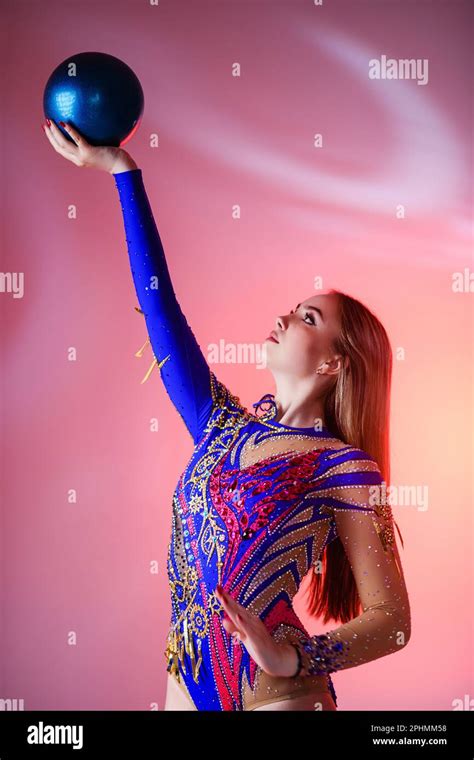 Girl Gymnast Wears A Gymnastic Leotard Practicing With A Ball On A Pink Background Stock Photo