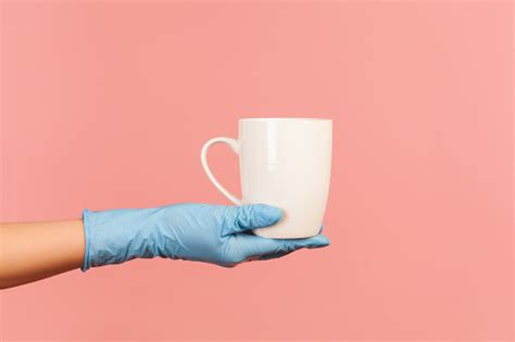 파란색 수술 장갑을 들고 손에 뜨거운 음료의 흰색 컵을 보여주는 인간의 손의 프로필 측면 보기 클로즈업 건강관리와 의술에 대한