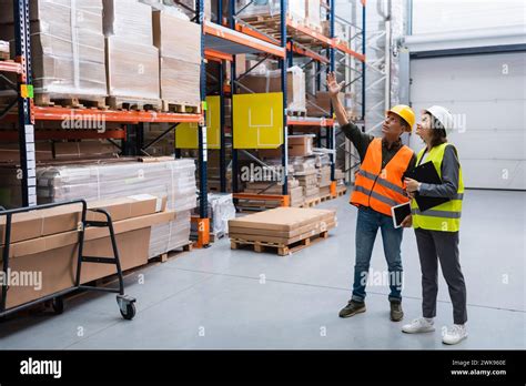 Cheerful Supervisor With Tablet Pointing Out Details To Female Employee In A Warehouse With