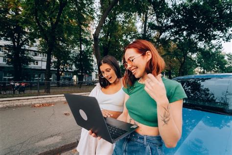 Dos Mujeres Jóvenes Con Una Computadora Portátil Cerca Del Auto Foto