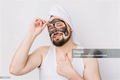 남성을 위한 스파 및 스킨 케어 흰색 배경에 그의 얼굴에 검은 안티 여드름 숯 마스크와 젊은 재미 남자 얼굴에서 마스크를