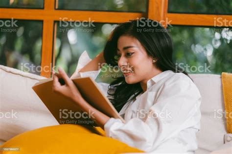 매일 책을 읽는 아름다운 젊은 아시아 여성 아늑한 집에서 조용한 시간과 편안한 환경을 즐기고 거실의 소파에서 휴식을 취하고