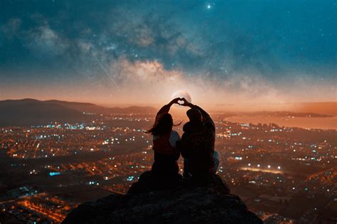 산 꼭대기에 앉아 도시의 달과 별을 배경으로 손으로 실루엣 하트 모양의 기호를 만드는 이성애 커플의 실루엣 뒷모습 커플에 대한