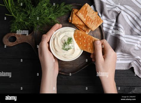 Woman Dipping Cracker Into Tasty Creamy Dill Sauce At Black Wooden