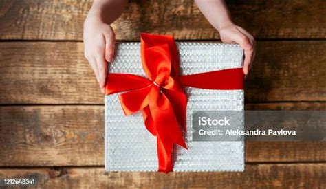 밝은 피부의 손에는 붉은 새틴 리본이 달린 커다란 흰색 선물 상자와 어두운 오래된 나무 배경에 커다란 활이 있습니다 0명에 대한 스톡 사진 및 기타 이미지 Istock