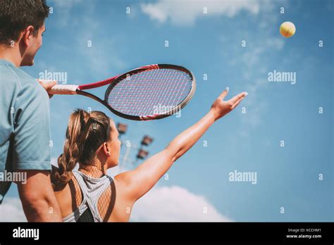 Beautiful Female Tennis Player With Instructor Practicing Serve On Outdoor Tennis Court Stock