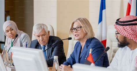 안경을 쓴 자신감 넘치는 성숙한 백인 여성이 다른 정치인들과 함께 테이블에 앉아 마이크를 사용하며 정치 회의에서 연설하고 있다 사진 Unsplash의 통신 이미지