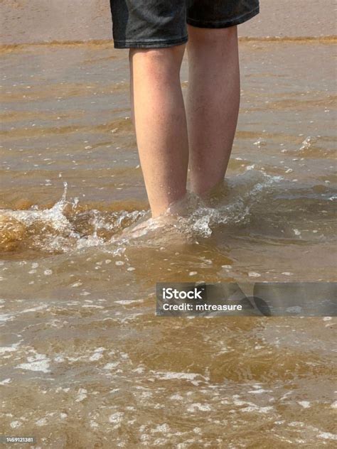 황금빛 해변 모래에 얕은 바닷물에 젖어가는 바다에서 노를 젓는 알아볼 수 없는 사람의 발 해안 해안선을 감싸는 파도 맨발로
