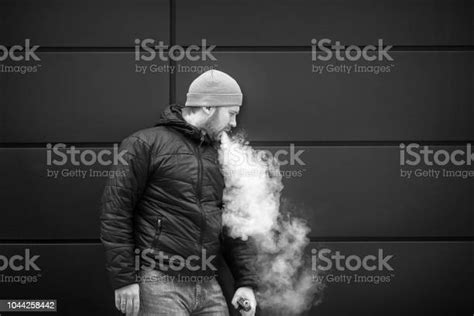 Vape 남자입니다 젊은 흰 수염 뚜껑에 사람이 전자 담배를 흡연 하 고는 증기 시키는 나쁜 습관입니다 흑인과 백인입니다 가을에