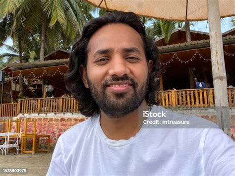 인도 남자의 클로즈업 이미지는 야외 식사 공간 해변 레스토랑 바에서 파라솔 아래에 앉아 카메라를 바라보며 전경에 초점을 맞춥니다 T 셔츠에 대한 스톡 사진 및 기타 이미지