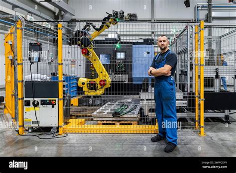 Young Maintenance Engineer Standing With Arms Crossed In Front Of Robotic Arm At Modern Factory