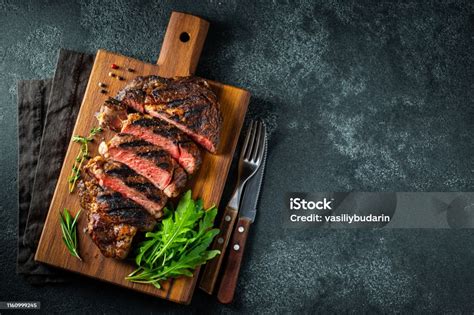 후추 마늘 소금 백리향으로 구운 얇게 썬 스테이크 리브아이는 어두운 돌 배경의 나무 도마위에 얹어 서빙됩니다 복사 공간이 있는 맨 위 뷰입니다 플랫 레이 고기에 대한 스톡