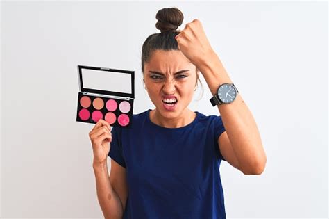 고립 된 흰색 배경 위에 서있는 메이크업을 들고있는 젊은 아름다운 여성은 화가 나고 화가 나고 미친 듯이 외치며 손을 들고 분노 개념을 고함칩니다 갈색 머리에 대한 스톡