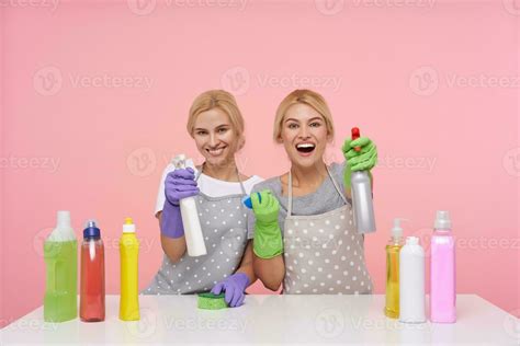 Happy Young Attractive Blonde Cleaning Ladies Dressed In Uniform Raising Hands With Spray