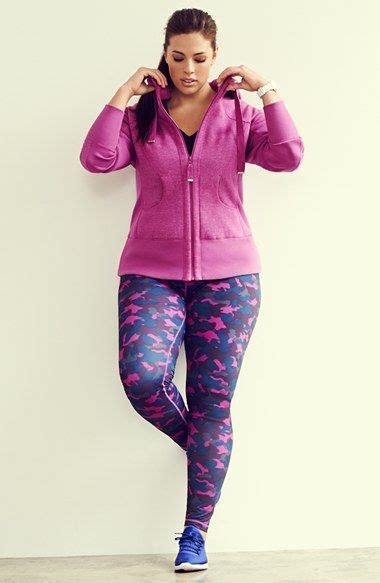 A Woman In Pink Jacket And Leggings Standing Next To White Wall With Her Hands On Her Head