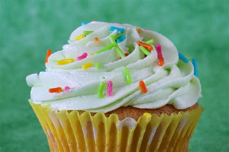 종이 케이크 케이스에 담긴 개별 바닐라 컵 케이크의 전체 프레임 이미지 민트 그린 버터 크림 아이싱 파이프 소용돌이 수백 수천 아이싱 스프링클 녹색 배경 전경에 초점 장식