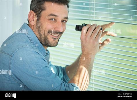 Excited Man Spying Through The Window Blinds With Binoculars Stock