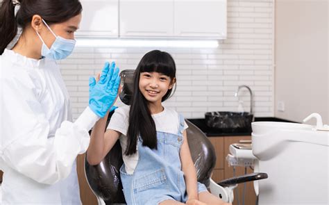 의자에 앉아 있는 어린 환자 소녀는 현대적인 장비를 갖춘 진료소에서 치과 치료를 받은 후 소아 치과의사에게 하이파이브를 한다
