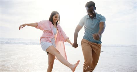 여행 목적지 여름 또는 신혼 여행을 위해 해변에서 인종 간 커플과 함께 웃고 손을 잡고 물놀이를 즐겨보세요 휴가 유대감 형성 또는 로맨스를 위해 남성과 여성과 함께 휴식을